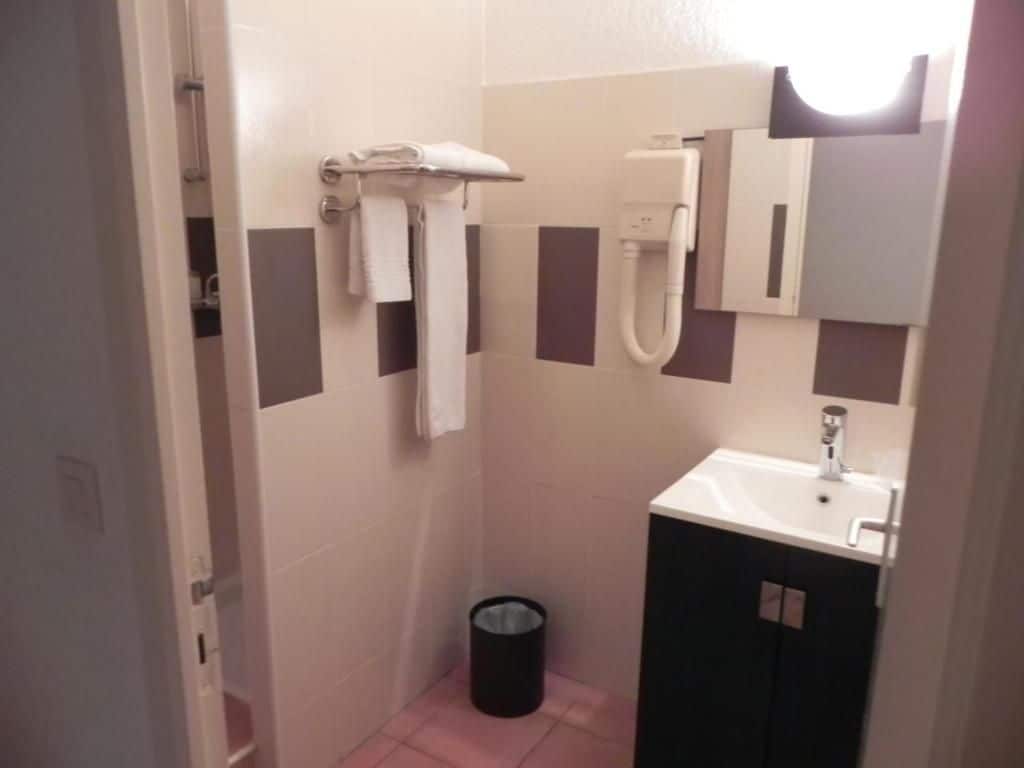 Casa de banho com lavatório, espelho, porta-toalhas e um cesto de lixo.