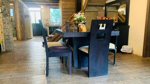 Uma sala de jantar com uma mesa e cadeiras de madeira, um vaso com flores e vista para a cozinha e sala de jantar.