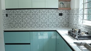 Uma cozinha com armários azul claro, um painel de parede estampado e uma janela com vista.