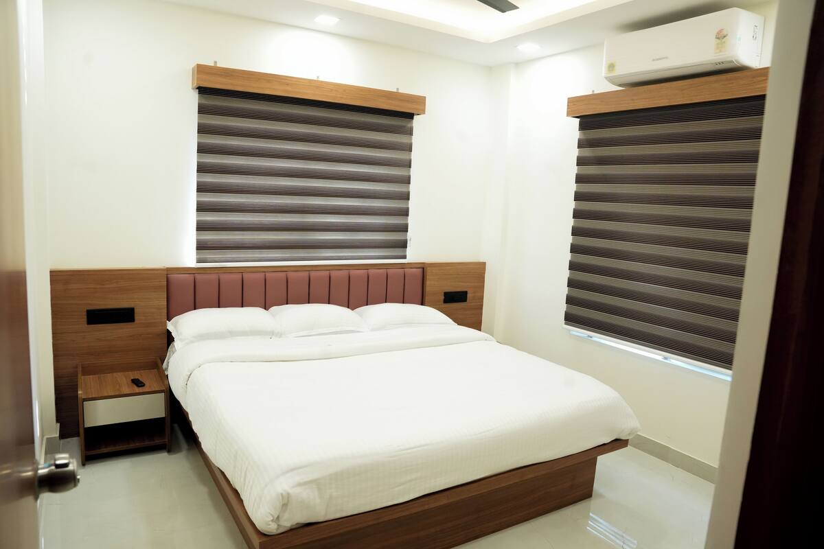 Quarto moderno com estrutura de cama de madeira, mesa de cabeceira e unidade de ar condicionado embutida.