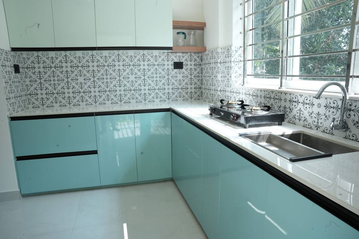 Cozinha com armários cor turquesa, pia de aço inoxidável e janela com vista para vegetação.