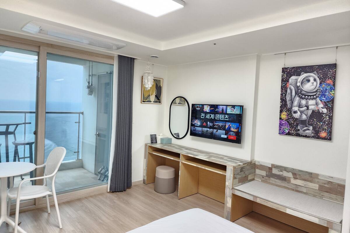 Quarto de hotel moderno com varanda, televisão na parede, secretária, cadeira e cama.