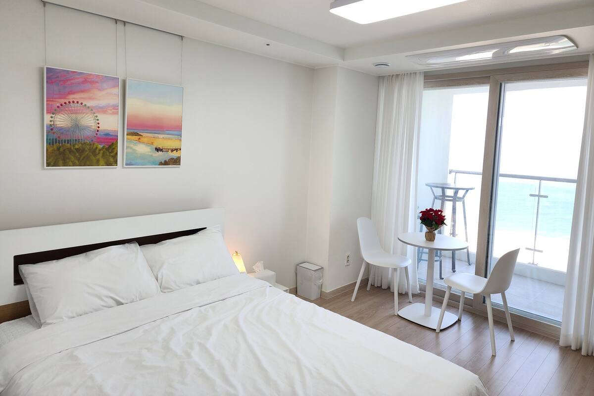 Quarto de hotel com cama, uma pequena mesa com cadeiras, uma varanda com vista e duas pinturas na parede.