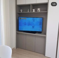 Uma TV fixada num móvel cinzento com vasos decorativos nas prateleiras acima.
