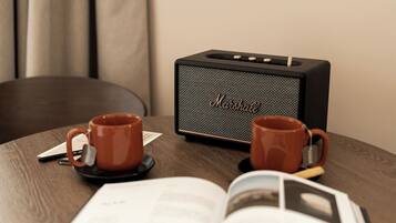 Uma mesa de madeira com um alto-falante Marshall, duas canecas, um livro e uma caneta.