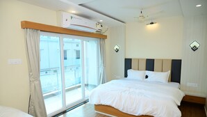 Quarto de hotel com uma cama grande, portas de vidro deslizantes para uma varanda, ventilador de teto e ar condicionado.