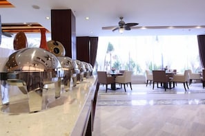 Uma área de buffet com várias estações de serviço e um espaço de estar com mesas e cadeiras.