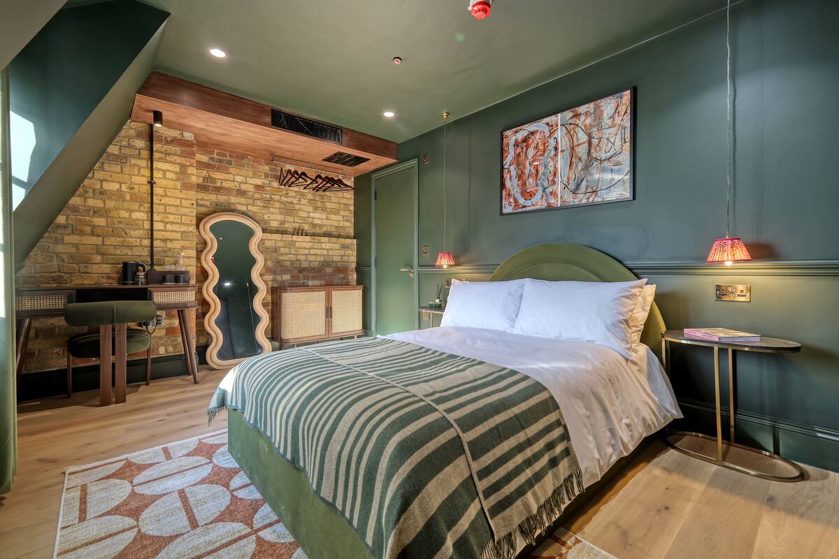 Quarto com cama, escrivaninha, cadeira, luminária e quadro na parede.