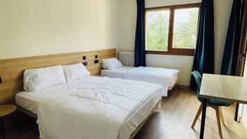 Quarto de hotel com duas camas, piso de madeira, janela com cortinas e uma mesa.