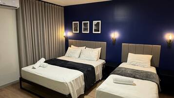 Quarto de hotel com duas camas, uma luminária de teto, ar condicionado e arandelas na parede.