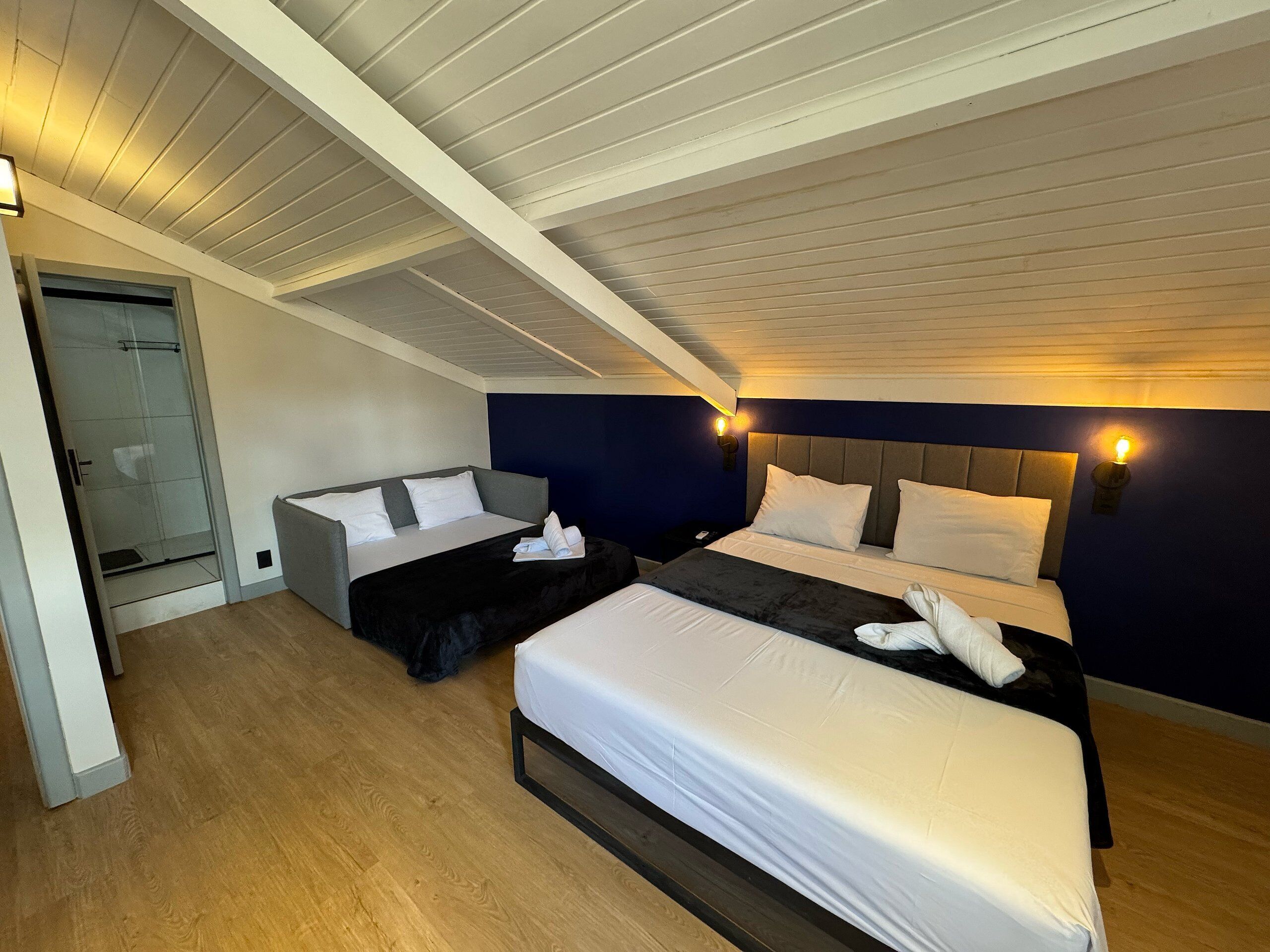 Quarto de hotel com duas camas, chuveiro e teto de madeira.
