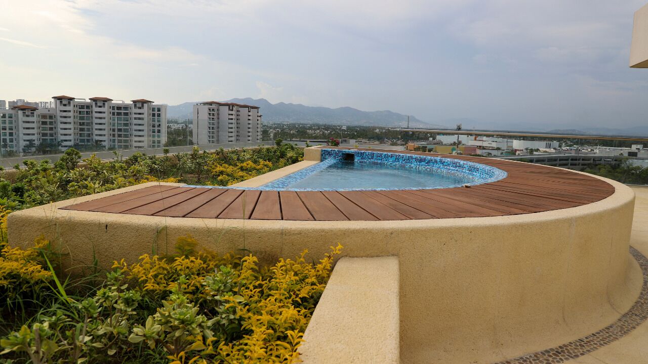 Uma piscina no terraço com um deck de madeira, rodeada por vegetação e uma paisagem urbana ao fundo.