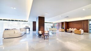 Um hall amplo com um sofá curvo, um piano e uma área de estar com móveis de vime.