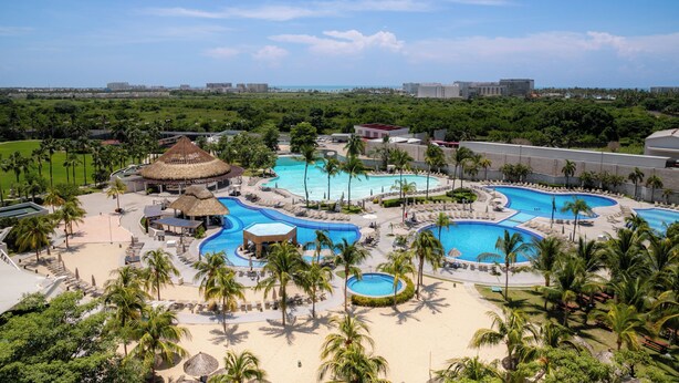 Resort com várias piscinas, palmeiras e área de praia.