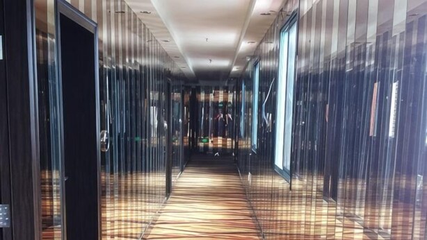 Um corredor com paredes de vidro, piso estampado e teto com iluminação embutida.