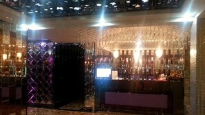 Uma área de bar com piso estampado, balcão com exposição e divisória de vidro decorativa.