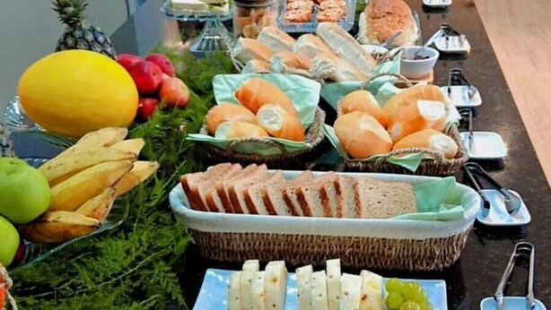 Buffet com diversas frutas, pães e sobremesas.
