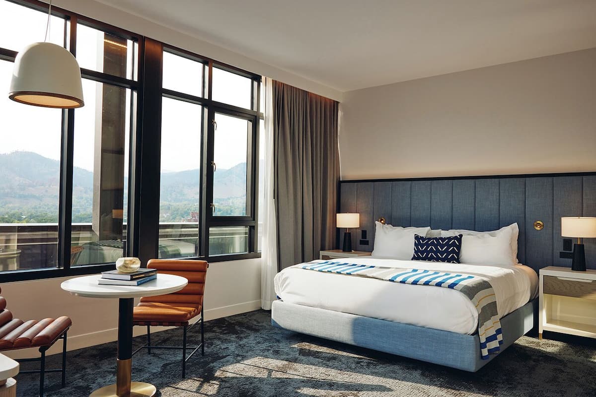 Quarto de hotel com uma cama grande, uma escrivaninha, uma cadeira e vista para as montanhas pela janela.