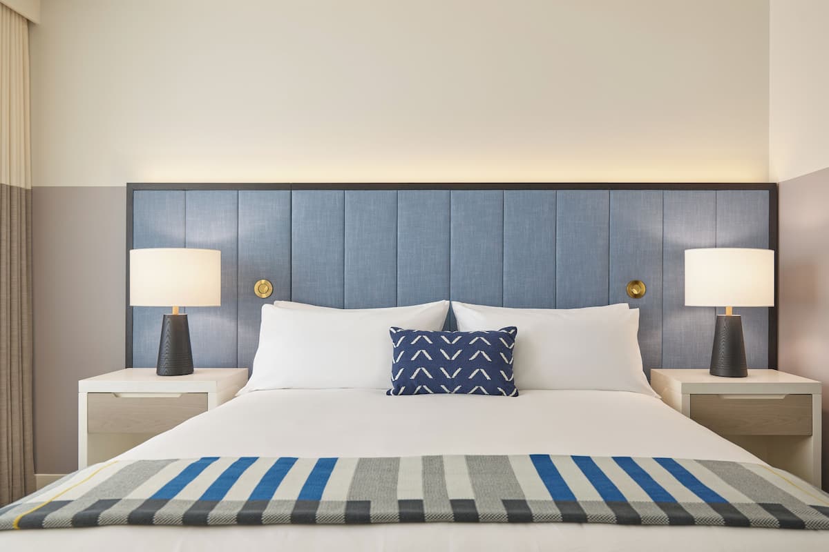 Quarto de hotel com uma cama grande, duas mesas de cabeceira, uma cabeceira e duas luminárias.