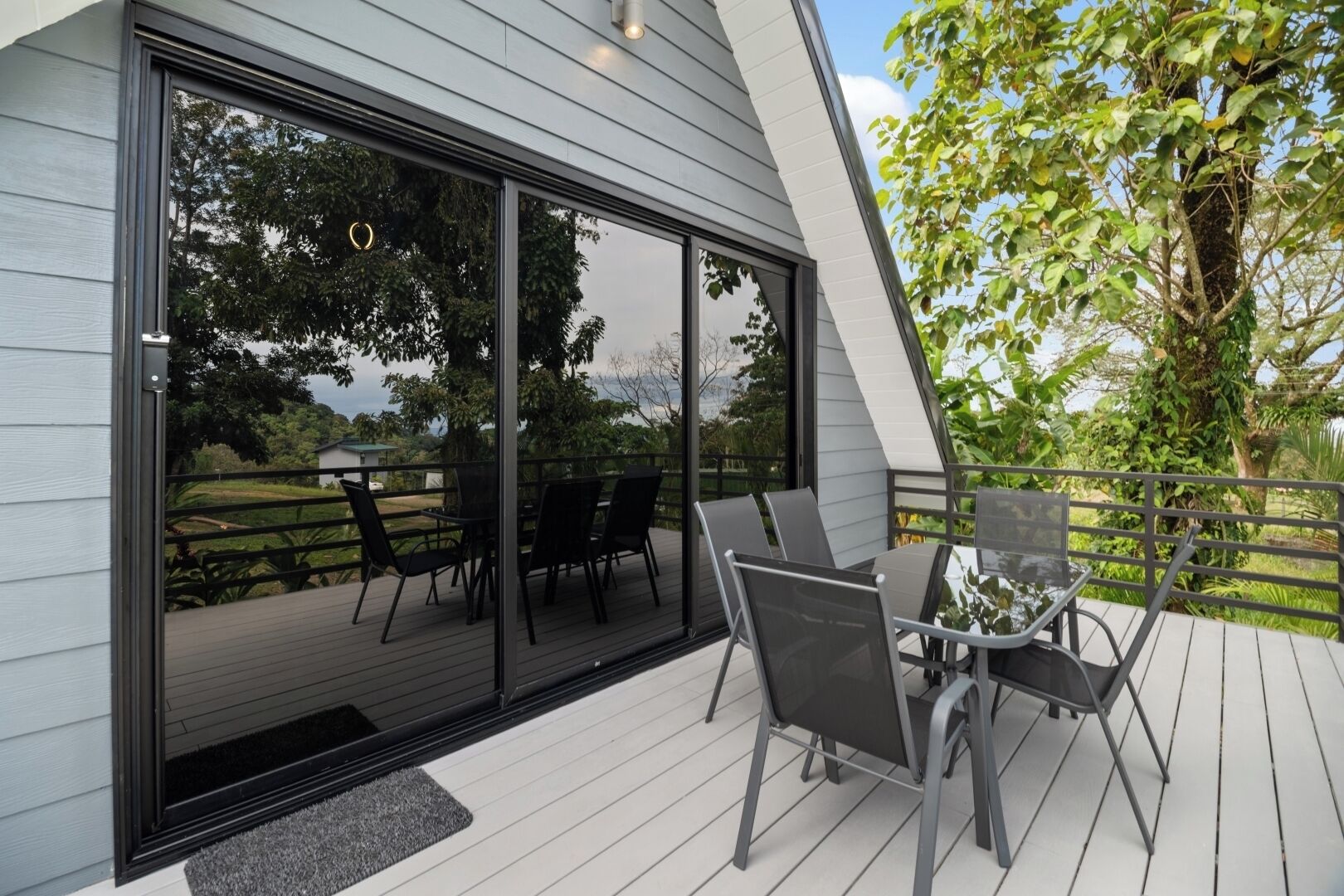 Uma casa moderna com um deck e porta de vidro que dá para uma área externa com cadeiras e uma mesa.