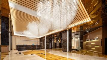 Um hall moderno com balcão de recepção em madeira, um lustre grande e piso de mármore.