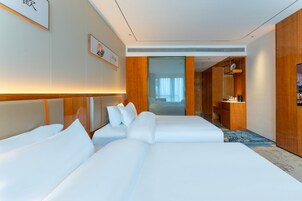 Quarto de hotel com duas camas, uma cabeceira de madeira, uma escrivaninha com cadeira e um espelho grande.