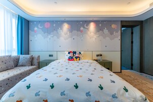 Quarto de hotel moderno com uma cama grande, um sofá, uma mesa de cabeceira e uma parede com um design de lua e estrelas.