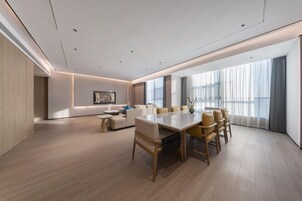 Uma sala de conferência moderna com uma mesa grande, várias cadeiras, um sofá e um amplo janelão com cortinas.