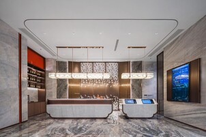 Um hall moderno com balcão de recepção, telas de informação digital e uma parede decorativa com padrão.