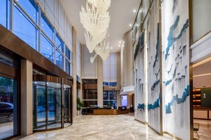 Um hall amplo com uma mesa de recepção, janelas grandes e um lustre moderno.