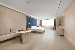 Quarto de hotel moderno com sofá, cama, mesa de jantar e guarda-roupa embutido.