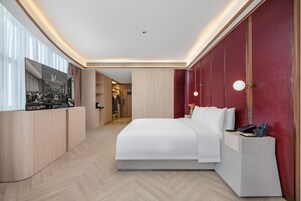 Quarto de hotel moderno com uma cama grande, uma escrivaninha com televisão de ecrã plano e uma toucador com espelho.