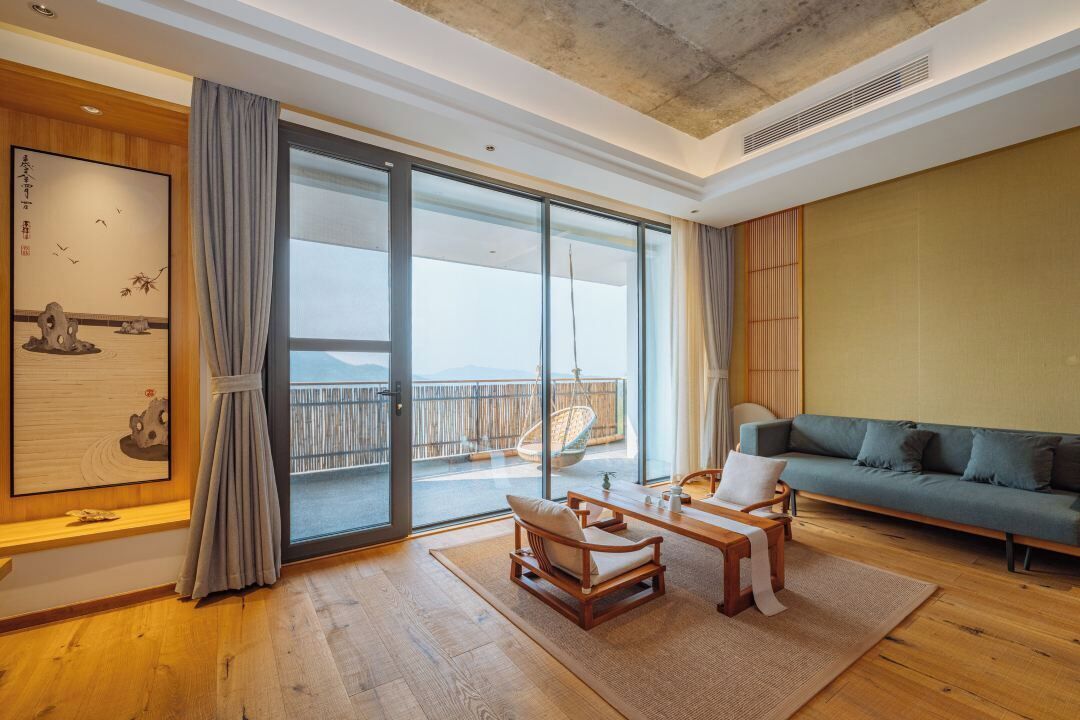 Uma sala de estar espaçosa com uma grande porta de vidro deslizante que dá para uma varanda, piso de madeira, um sofá verde e uma mesa de centro de madeira.