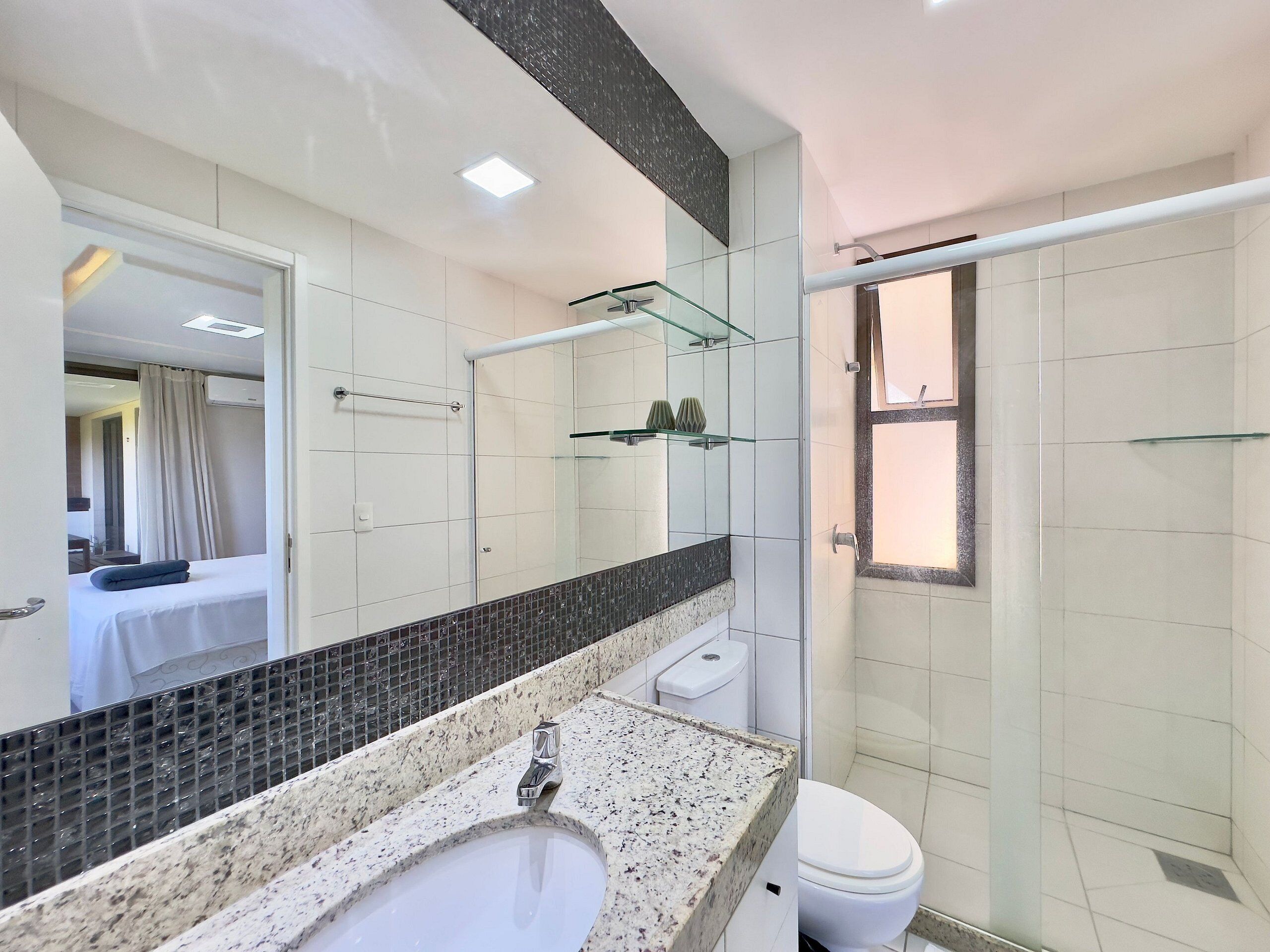 Um banheiro moderno com pia de bancada de granito, box de vidro e vaso sanitário branco.