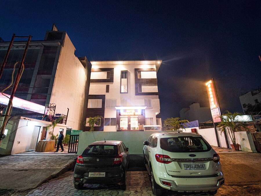 Um hotel com fachada moderna, uma entrada bem iluminada e dois carros estacionados em frente.