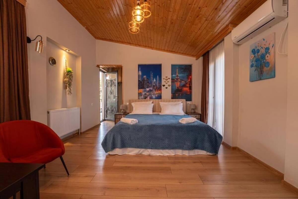Quarto com teto de madeira, cama com manta azul, cadeira vermelha e obras de arte nas paredes.