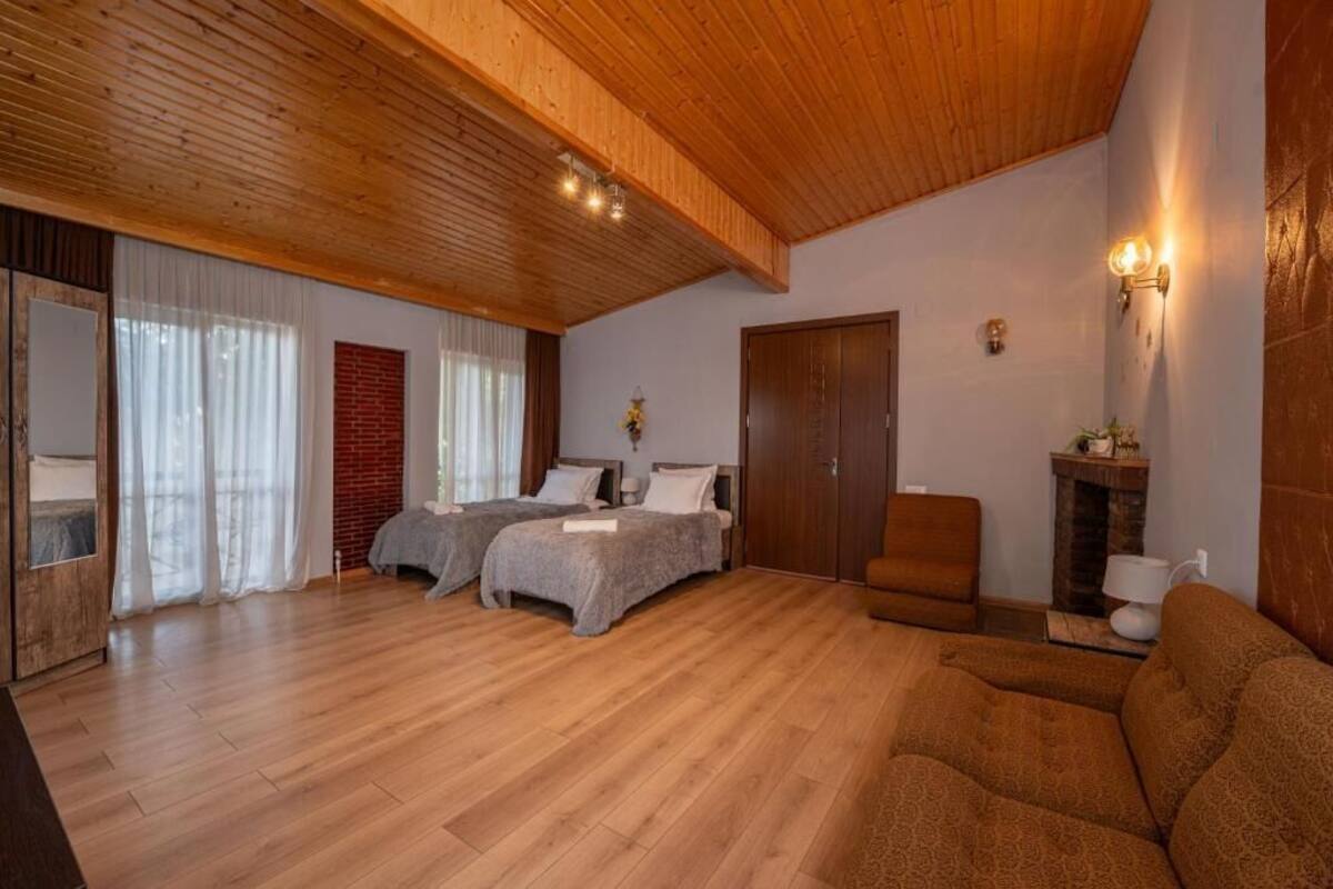 Um quarto amplo com piso de madeira, duas camas, um sofá, uma lareira e uma janela grande com cortinas.