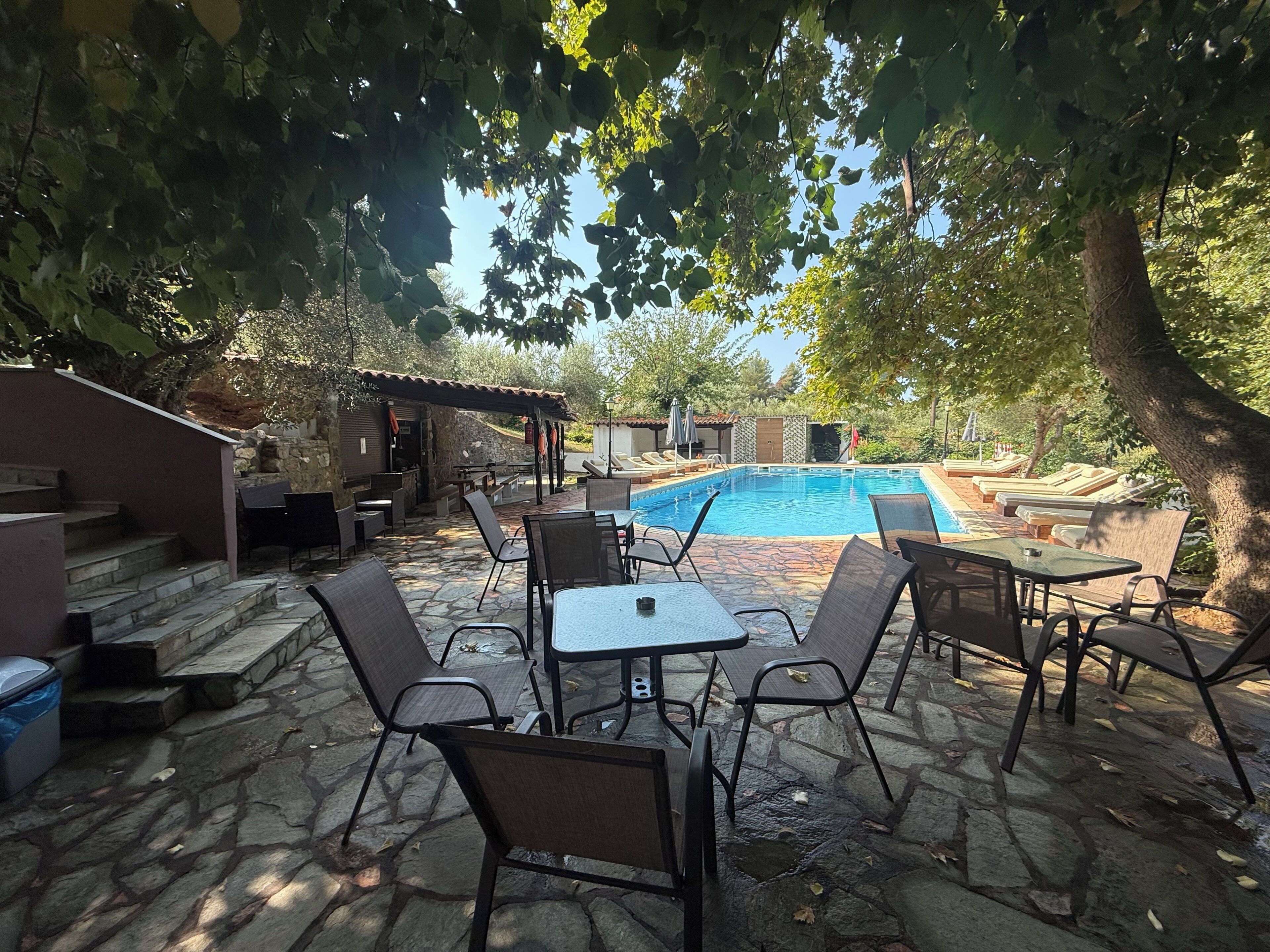 Uma área de piscina ao ar livre com piso de pedra, espreguiçadeiras e um espaço de estar coberto.