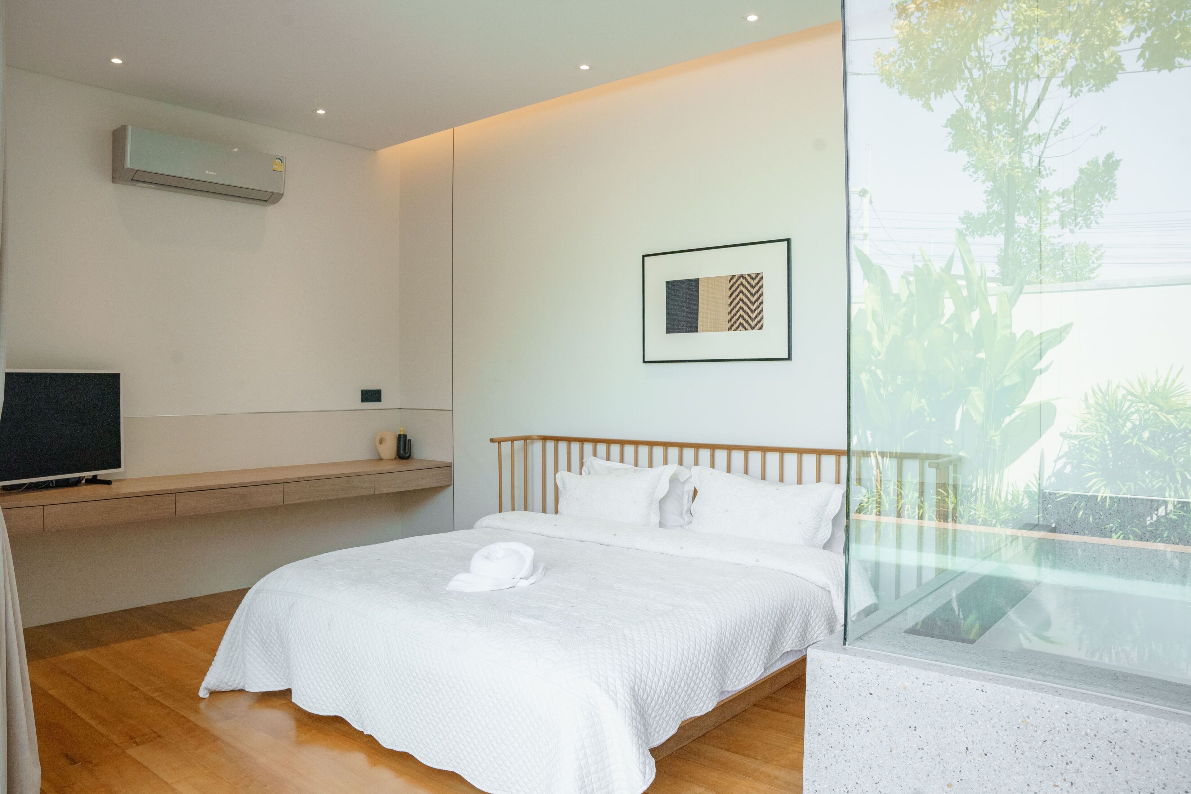 Quarto moderno com cama, televisão montada na parede, quadro emoldurado e varanda com plantas.