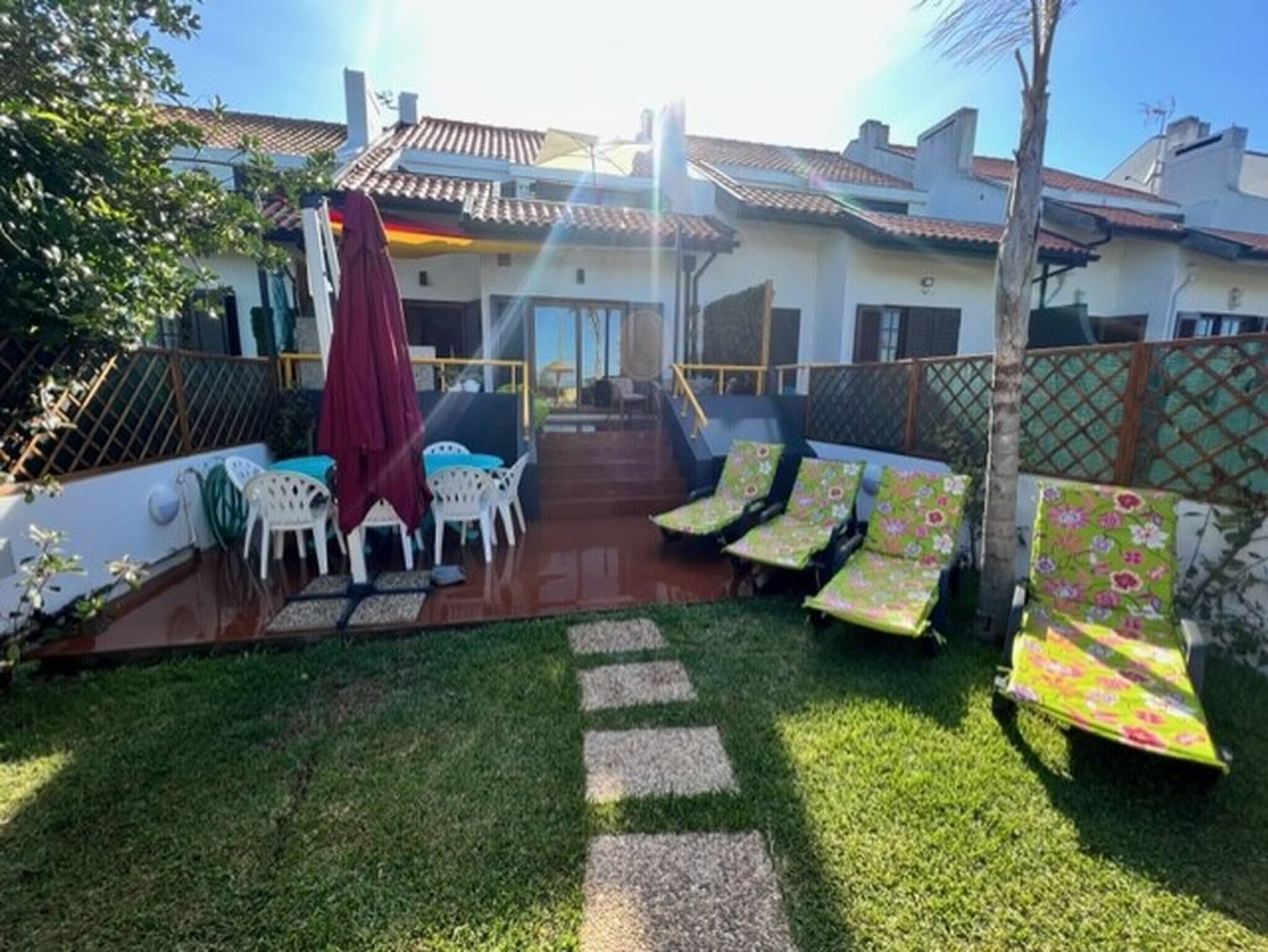 Uma área de pátio com espaço para sentar, uma mesa coberta e vista para uma casa com telhado de telhas.