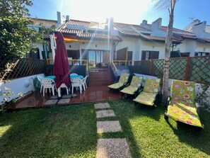 Uma área de pátio com espaço para sentar, uma mesa coberta e vista para uma casa com telhado de telhas.