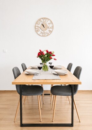 Uma mesa de jantar com seis cadeiras, um vaso de flores e um relógio de parede.