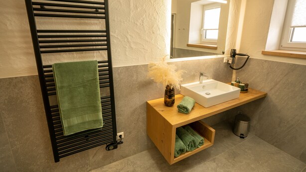 Uma casa de banho moderna com toucador de madeira, uma pia branca, um porta-toalhas e um espelho.