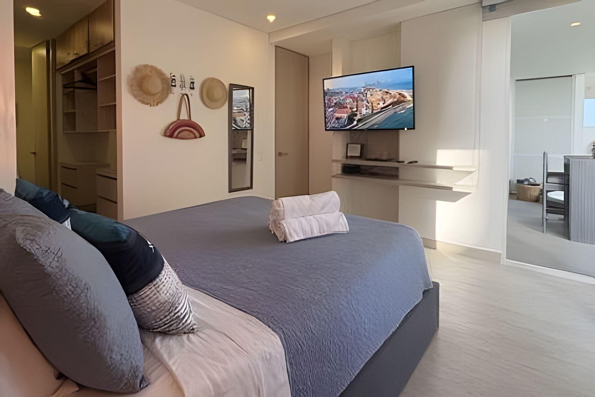 Quarto moderno com uma cama grande, uma televisão na parede e vista para a cidade.