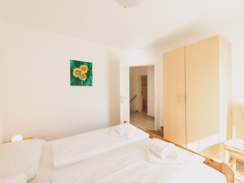 Quarto de hotel com duas camas, um guarda-roupa de madeira, um quadro de girassóis e vista para o corredor.