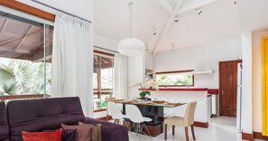 Um espaço de estar moderno com área de refeições, cozinha e janelas amplas.