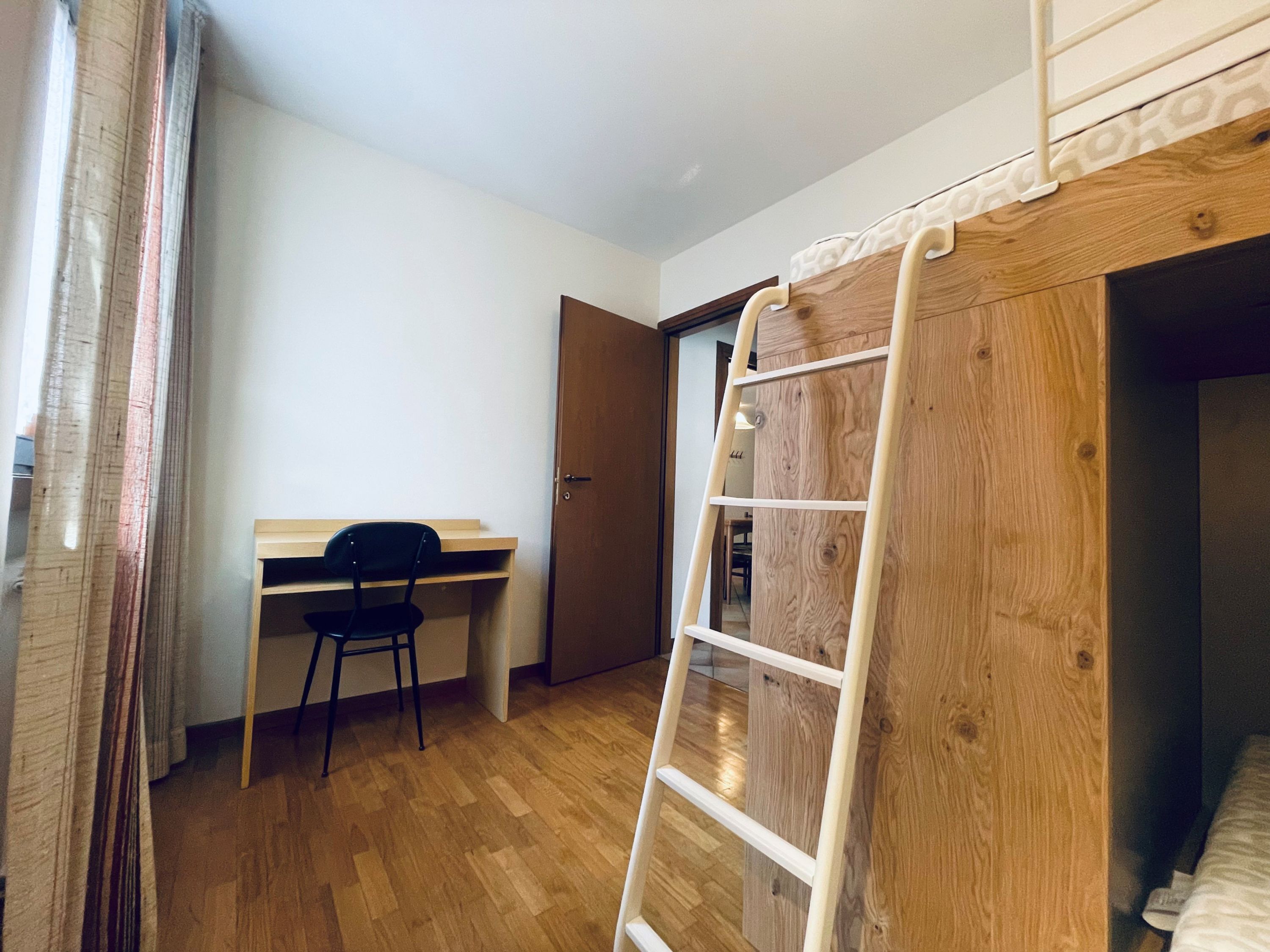 Um quarto com uma escrivaninha de madeira, uma cadeira preta, uma escada e uma cama.
