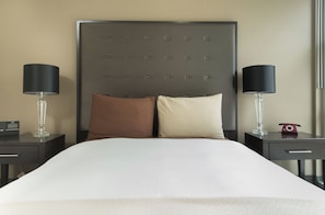 Quarto de hotel com uma cama grande, duas mesas de cabeceira, um telefone e uma luminária em cada lado.
