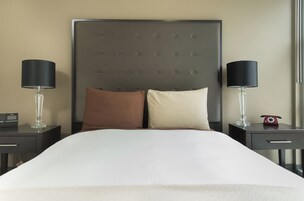 Quarto de hotel com uma cama grande, duas mesas de cabeceira, um telefone e uma luminária em cada lado.