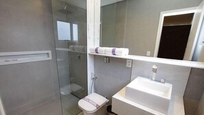Um banheiro moderno com box de vidro, pia branca e vaso sanitário.